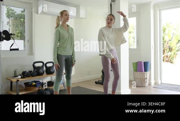 Female friends performing side-neck stretch on gym mat after instructor ...