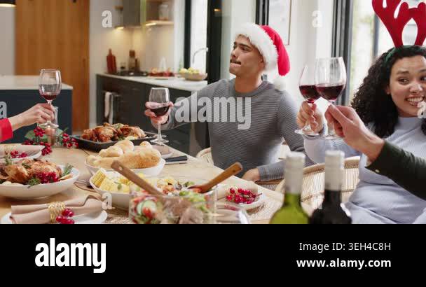 Diverse friends raising wine glasses following man lifting glass at ...