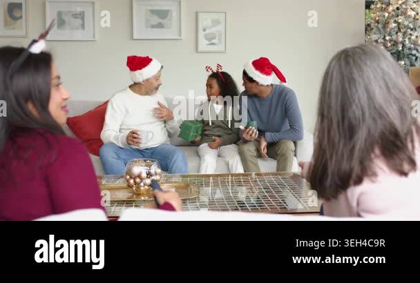 Diverse family watching grandpa urging child unwrapping green gift box ...
