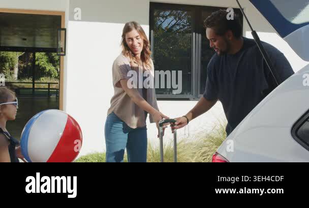 Family loading suitcase in driveway by car, parents handling luggage ...