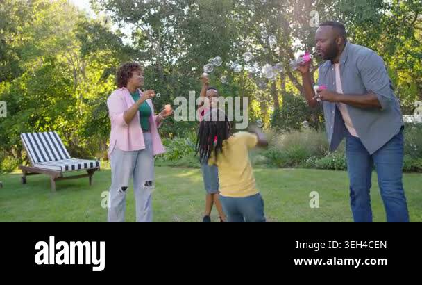 African American family parents blowing bubble wands, kids chasing ...