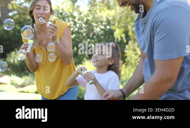 Family of 3 on sunlit lawn woman raising bottle dipping wand blowing ...