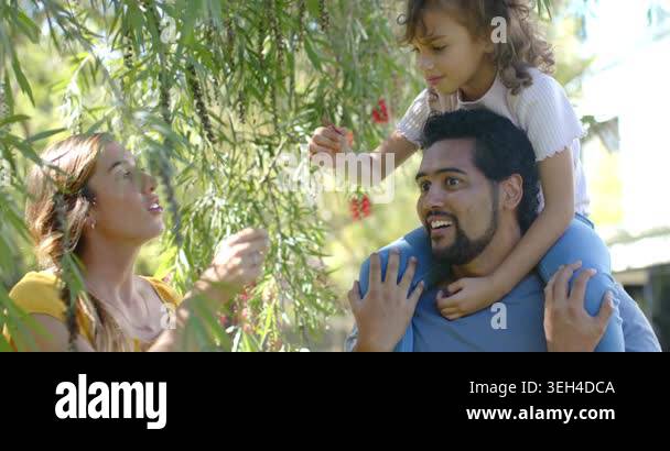 Diverse family dad holding child on shoulders, yellow-top mom reaching ...