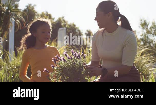 African American mother and daughter gesturing at plant and sniffing ...