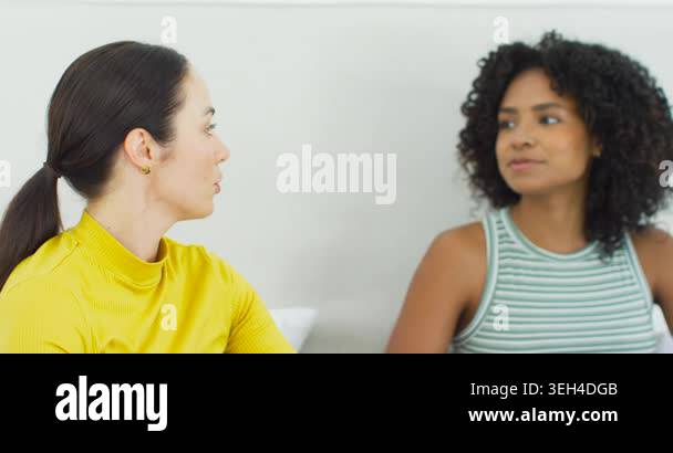 Female friends talking on couch with pillow, yellow top asking, striped ...
