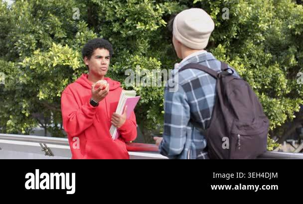 Diverse male friends leaning on campus path railing eating apple after ...