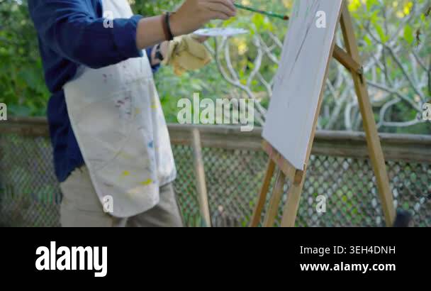 Senior Asian painter wearing stained apron mixing on palette, painting ...