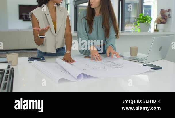 Diverse female colleagues unrolling plans, smoothing at white counter ...