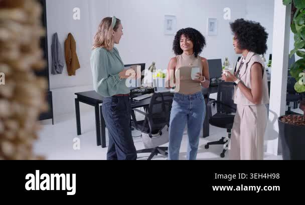 Diverse female colleagues with coffee mugs, center woman starting chat ...