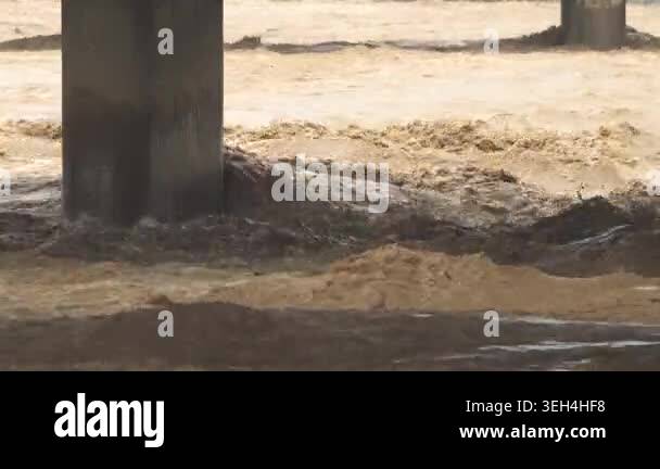Fast floodwater surges between concrete bridge columns with muddy ...