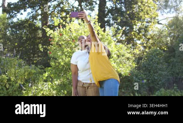 Mother and daughter in sunlit garden, right woman raising purple ...