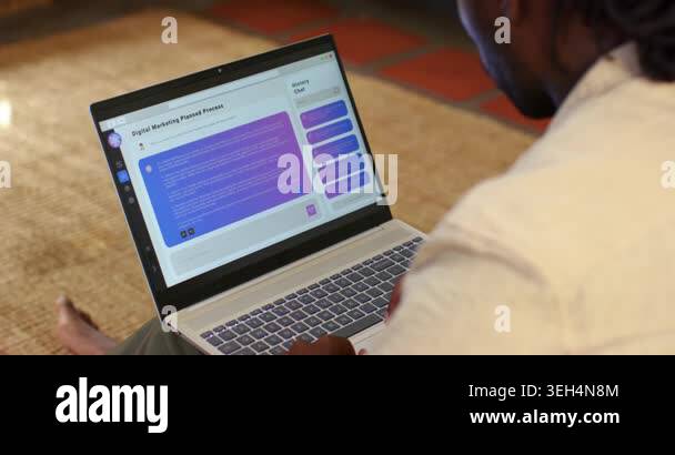 African man on rug opening laptop, reading marketing plan, typing ...