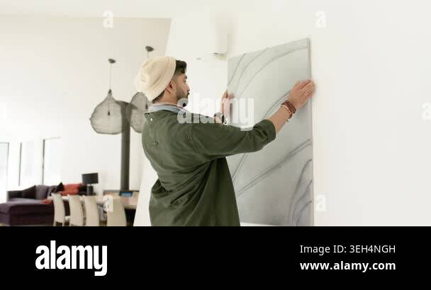Adult male entering living area carrying abstract canvas, aligning it ...