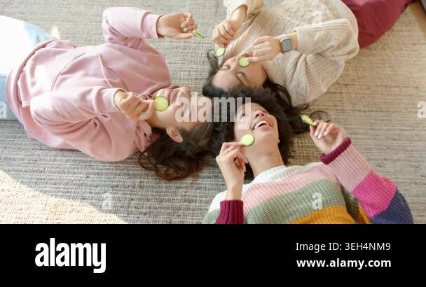 Diverse female friends lying on rug at home placing cucumber slices on ...