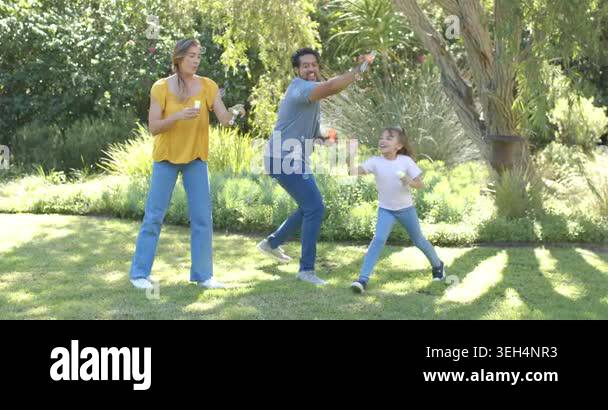 Diverse family playing mom lifting wand blowing bubbles, dad tossing ...