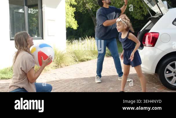 Diverse family passing bright beach ball on driveway by open white ...