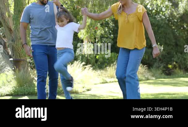 Diverse family parents bending, lifting and swinging child by hands on ...