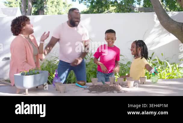 African American family gathering, potting seedlings at backyard table ...