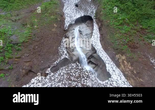 Aerial meltwater stream cuts through old avalanche snow on a forested ...