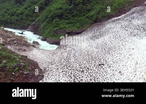 Aerial meltwater stream cuts through old avalanche snow on a forested ...