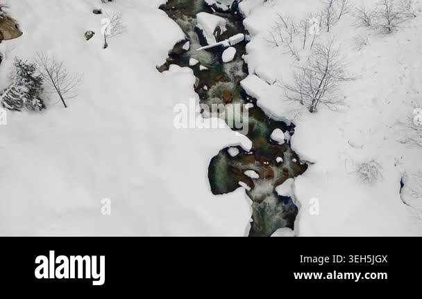 Aerial mountain stream winding through deep snow tunnel in winter ...