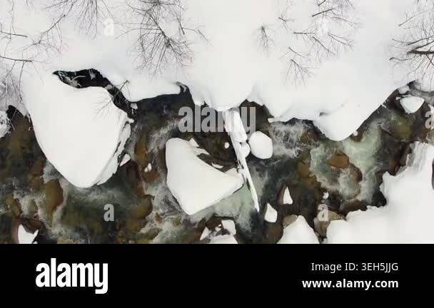 Aerial mountain stream winding through deep snow tunnel in winter ...