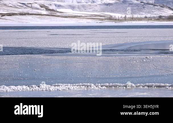 Frozen water surface holds ice sheets and cracks, winter stream or lake ...