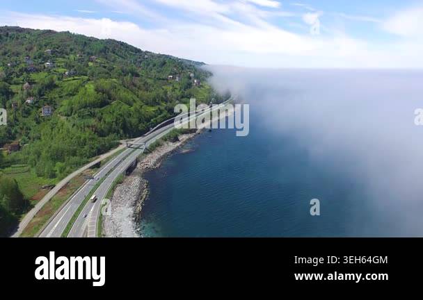 Aerial coastal highway along forested shoreline beside calm sea ...