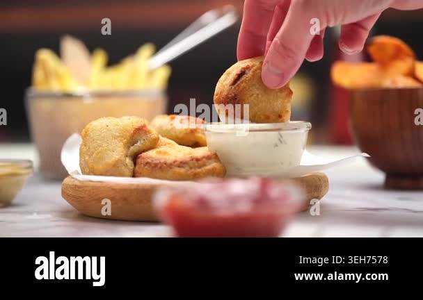 Crispy golden chicken nuggets served on wooden plate with white sauce ...