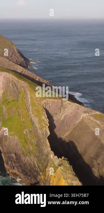 Sheer, layered rock formations plunge into the deep blue, restless sea ...