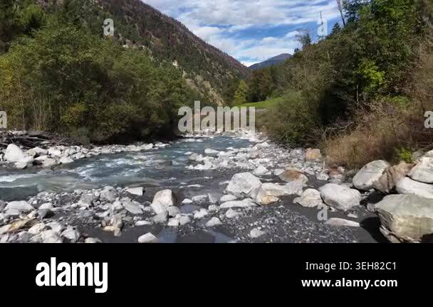 Turquoise mountain river flows over pebbles and rocks through a lush ...