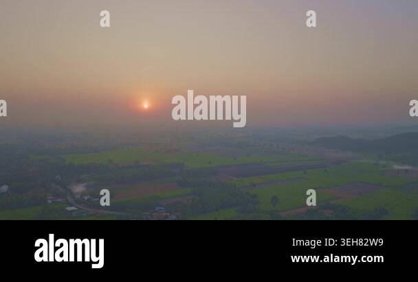 Sun setting over a vast landscape with green fields and a hazy sky ...