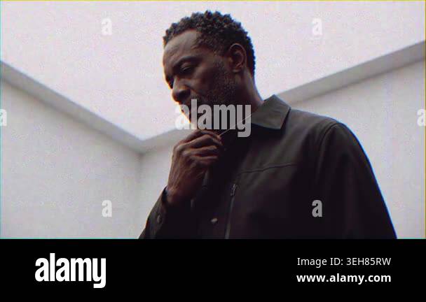 Black man under skylight adjusting necklace, veteran actor reflecting ...