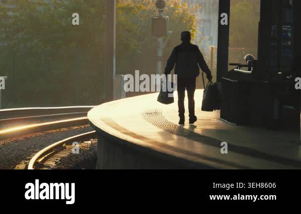 A man carries two bags as he walks beside train tracks at a city ...