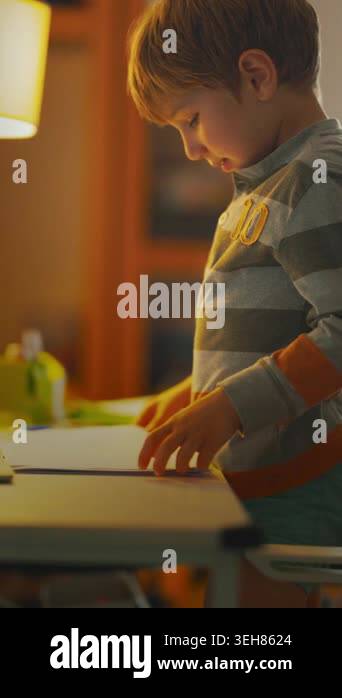 A young child stands at a table and draws on a piece of paper in the ...