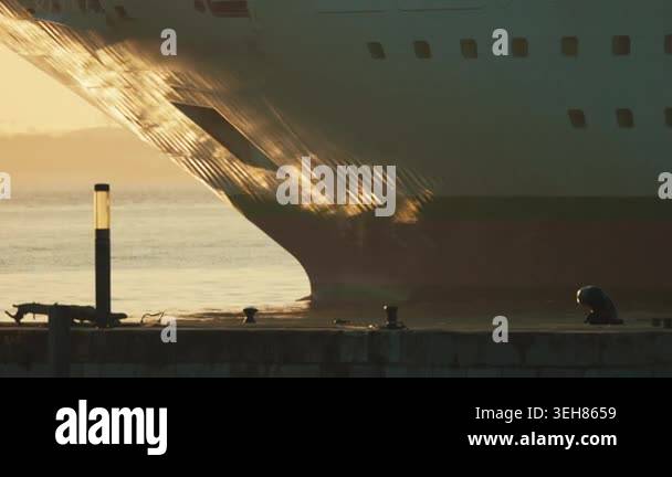 A large ship is docked in the harbor as the sun sets. Reflections ...