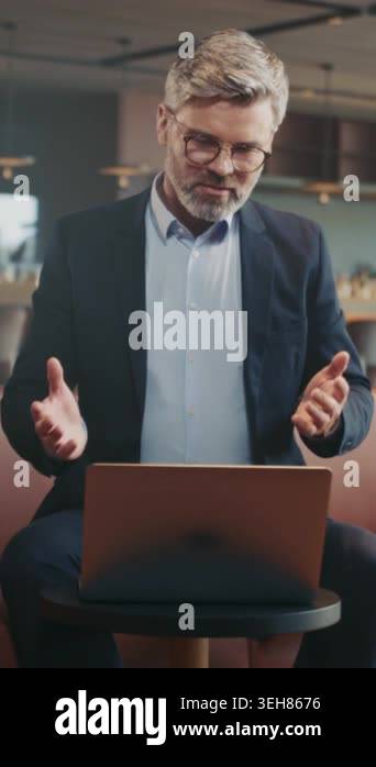 mature caucasian executive presenting to camera with laptop, gesturing ...