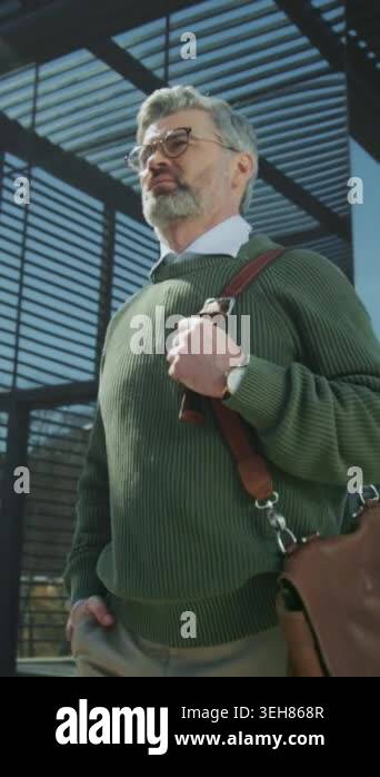 gray haired white executive under canopy, striding with leather ...