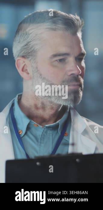 Mature white doctor analyzing tablet data inside research lab, wearing ...