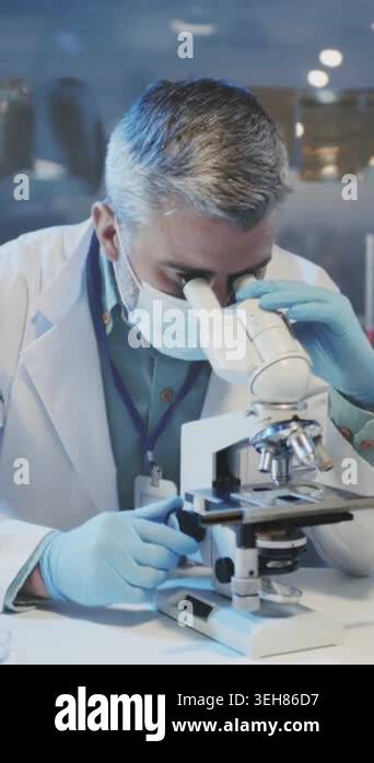 Caucasian researcher examines slide under microscope in modern ...