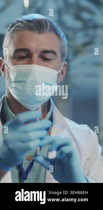 white male doctor preparing vaccine vial, masked physician inspects ...
