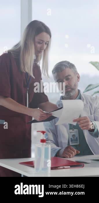 white nurse presenting report to doctor, standing over seated senior ...