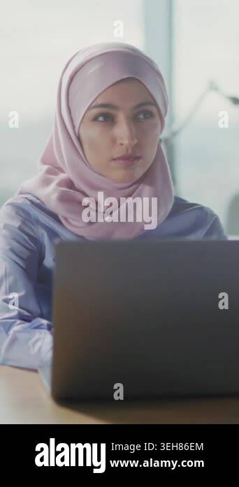 woman with headscarf at laptop focused on analytics and reports, bright ...