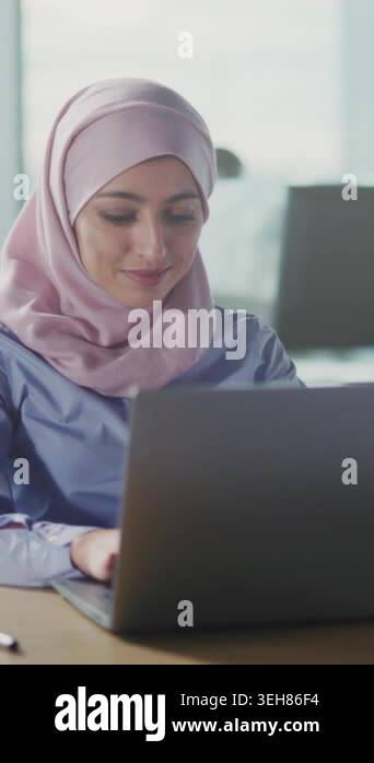 woman with headscarf at laptop celebrating online success with bright ...