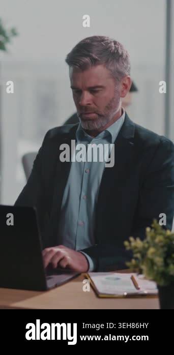caucasian executive at laptop focused, glass office with cityscape ...
