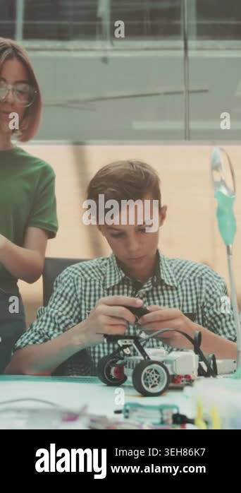 student assembles robot car at table, collaborative workshop scene with ...