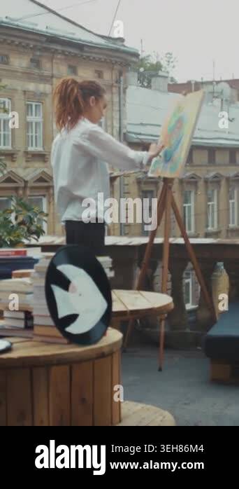 young woman painting on rooftop balcony capturing colorful cityscape on ...