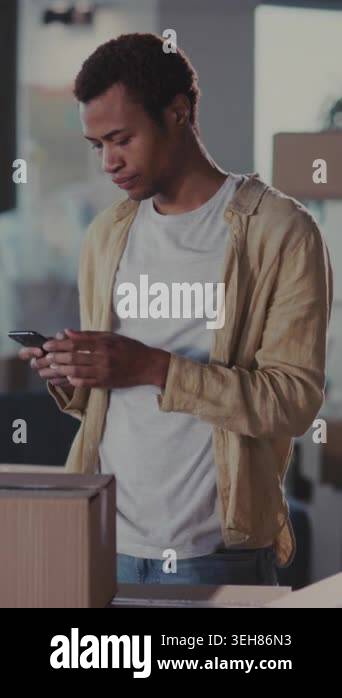 Black man checking smartphone while packing orders, focused expression ...
