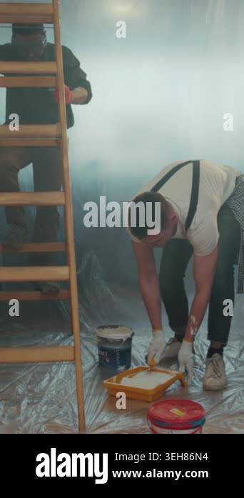 white men prepping paint tray and ladder in covered room, handing tools ...