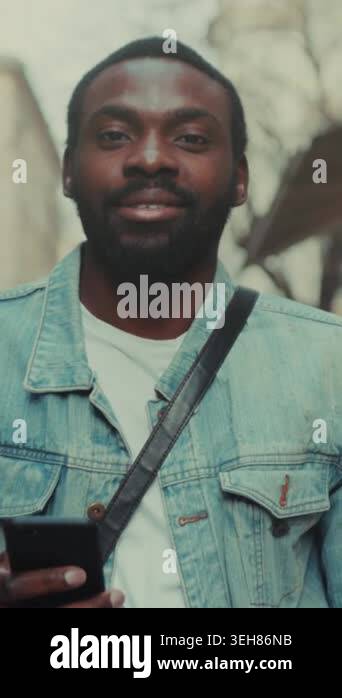 Black man in denim checking phone, quiet city street scene with soft ...